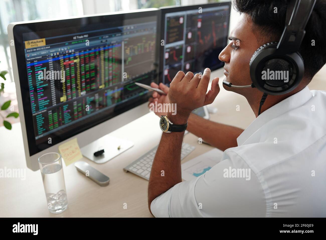 Serious trader in headset checking financial graphs on computer screens ...