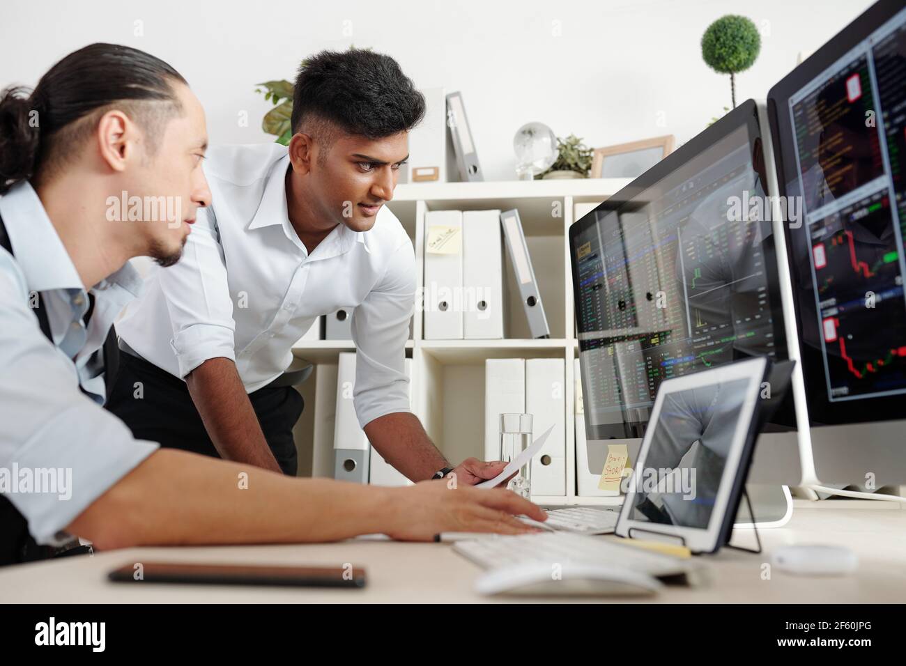 Multi-ethnic team of traders monitoring stock market data on computer ...