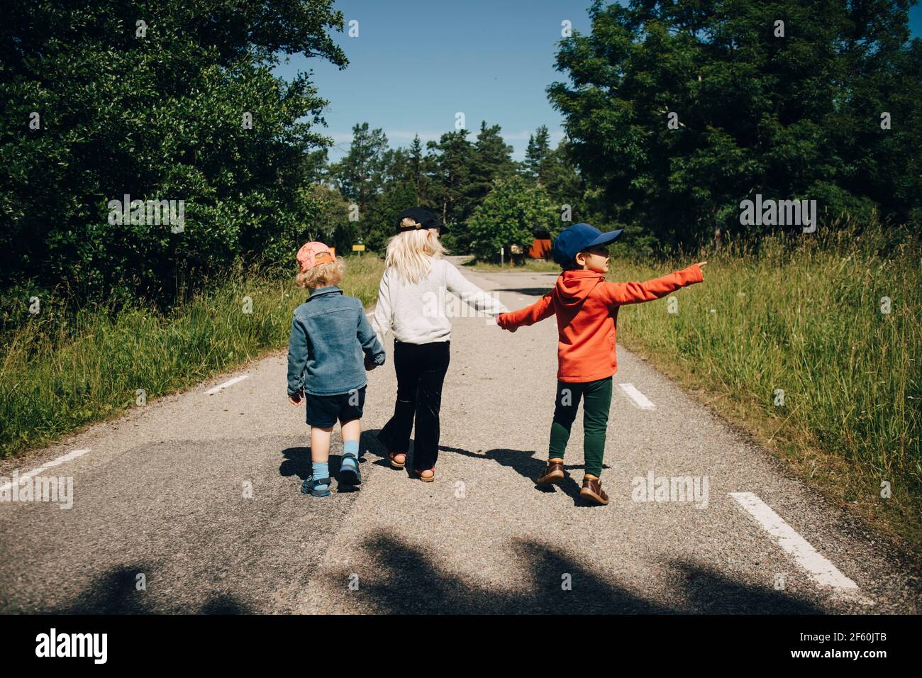 Rear view of sister with brothers walking on road during sunny day ...