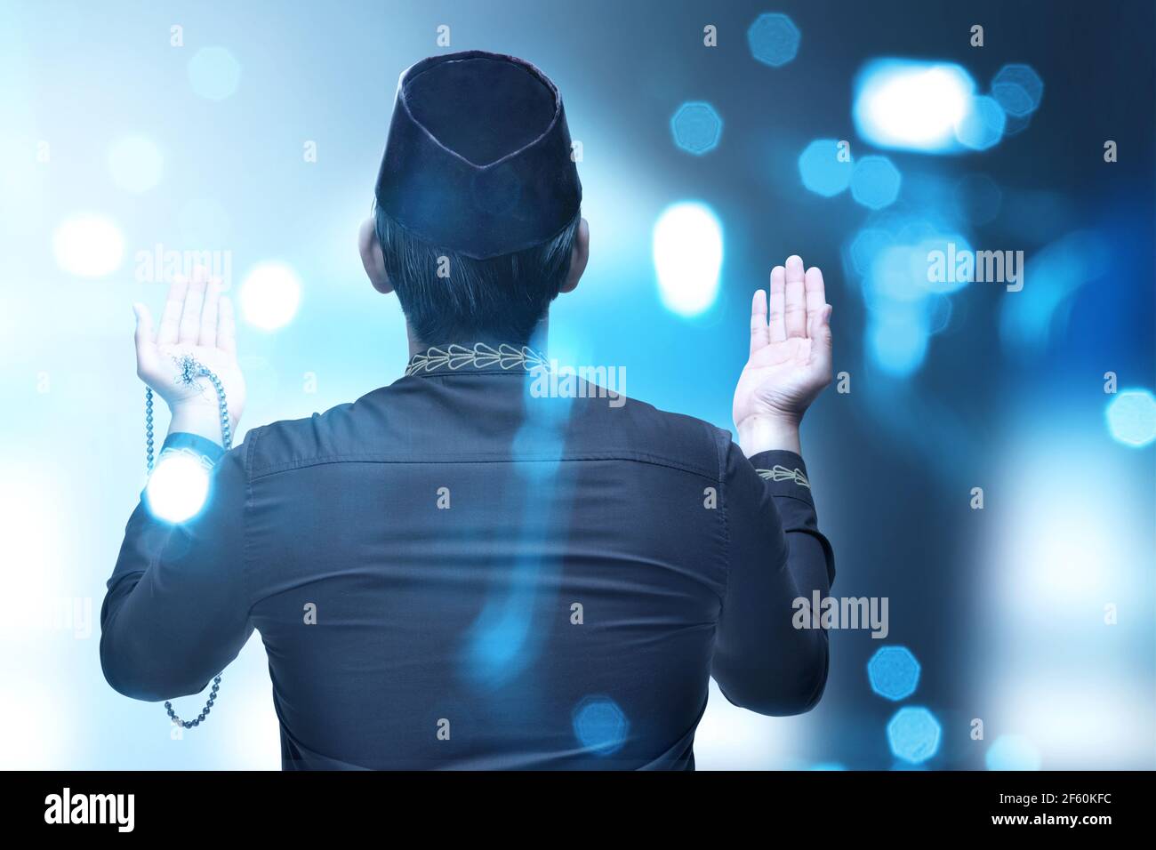 Rear view of Asian Muslim man praying with prayer beads on his hands ...