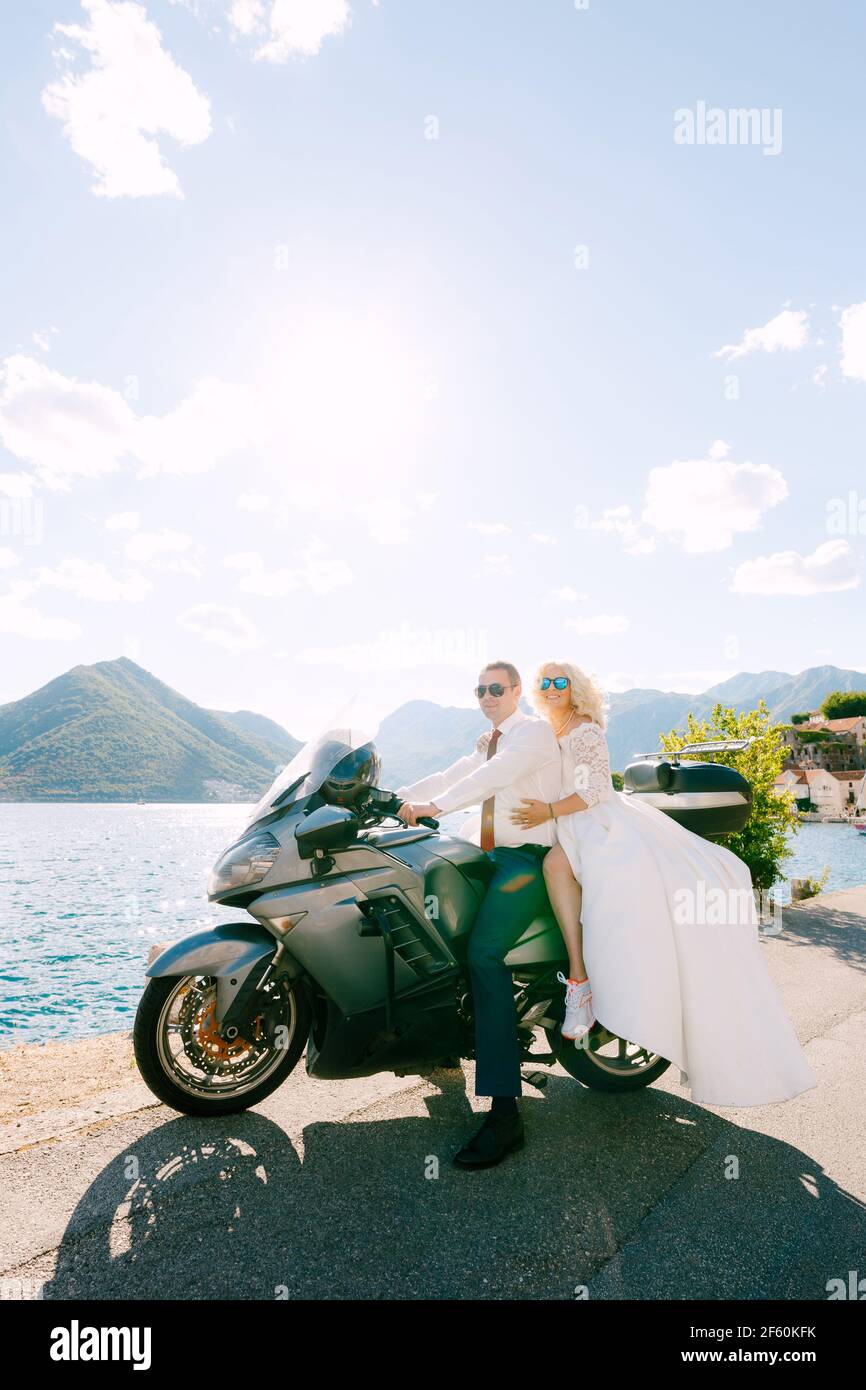 The bride and groom sit on a motorcycle on the pier in Perast, the ...