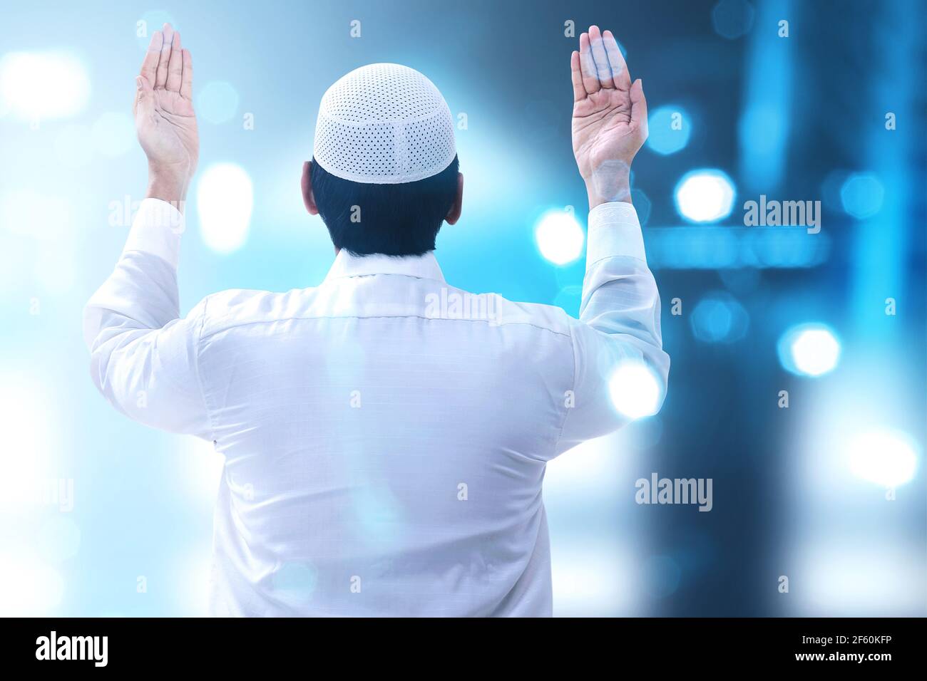 Rear view of Asian Muslim man standing while raised hands and praying ...
