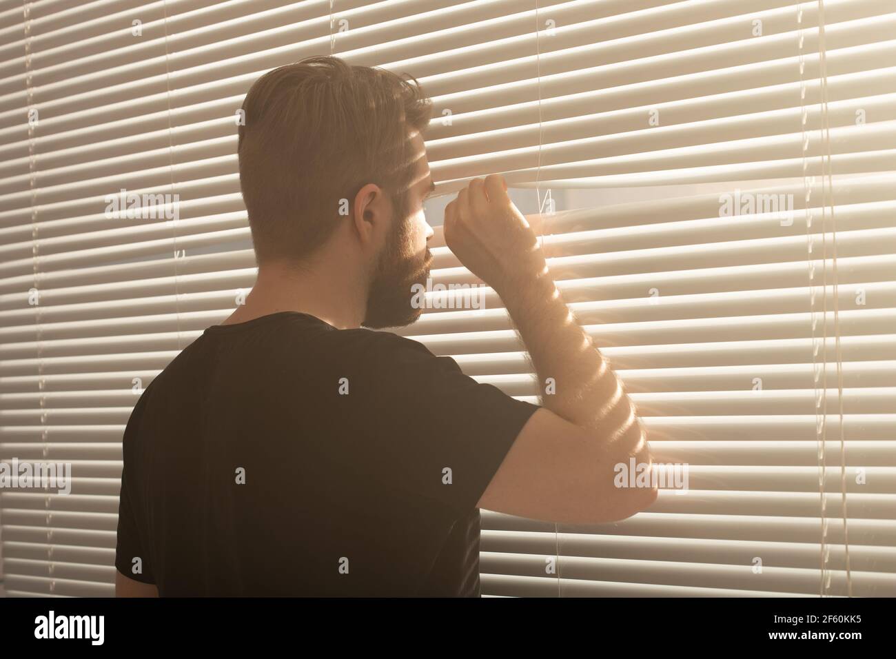 Rear view of young man with beard peeks through hole in the window ...