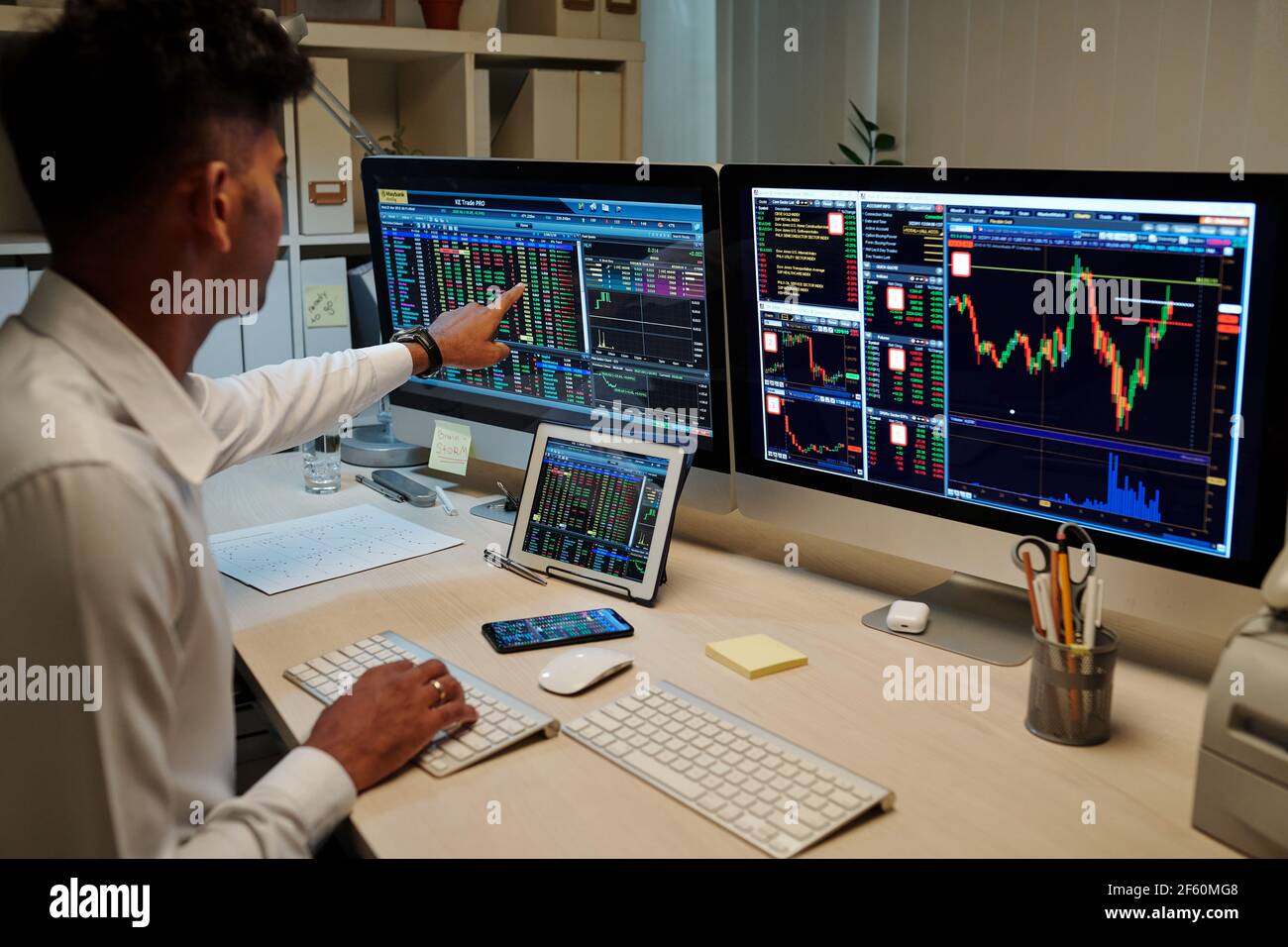Professional young Indian trader working in dark office and pointing at ...