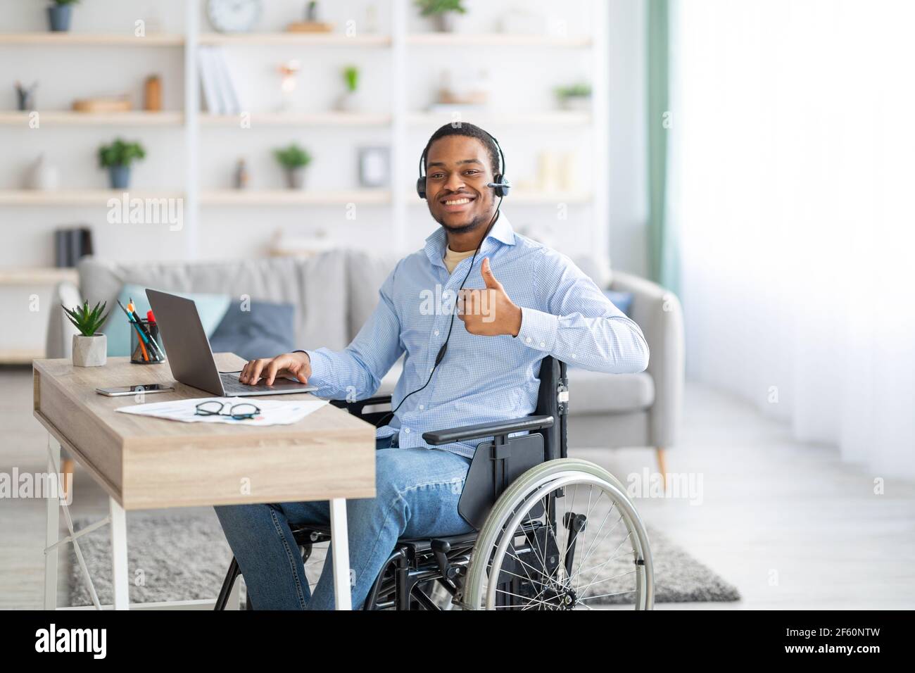 Positive disabled black man in headset using laptop computer for online ...