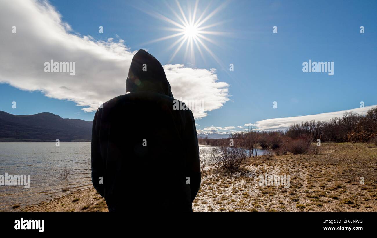 Hooded person with his back to a swamp with wet ground and mountains in ...