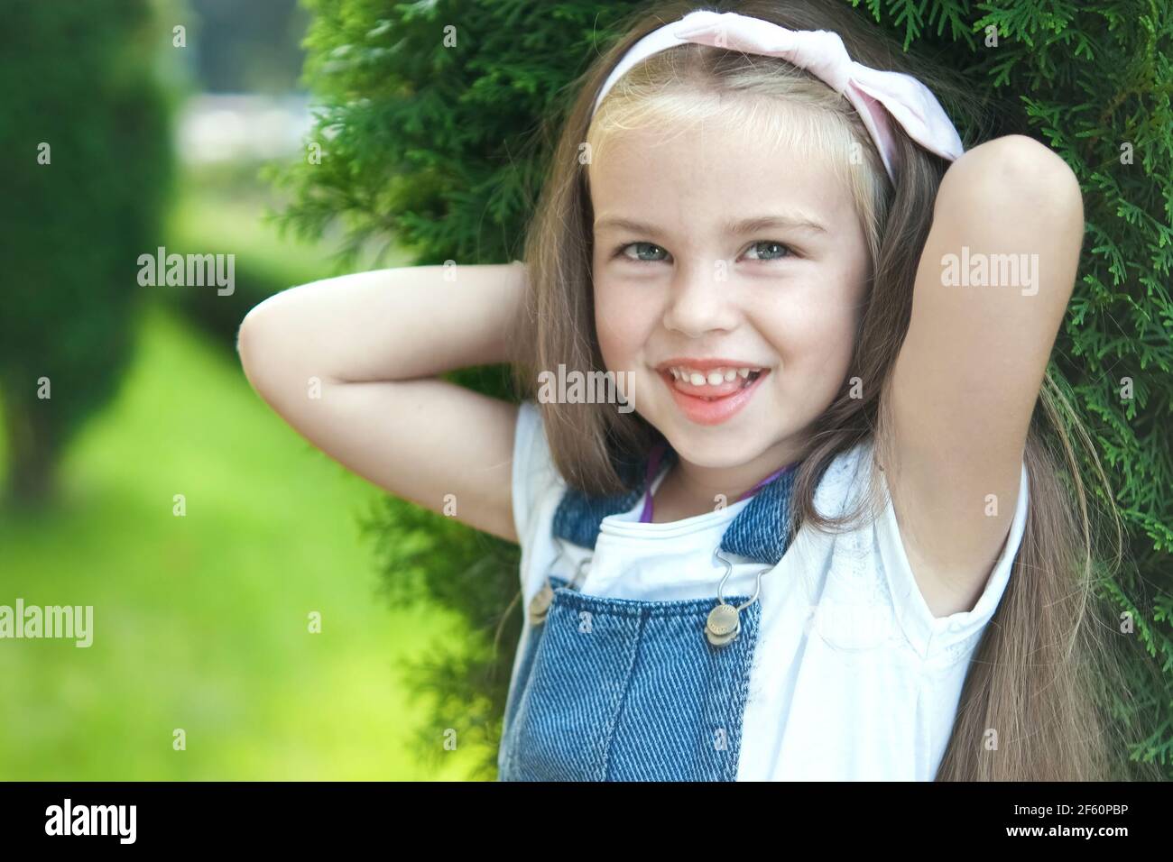 Portrait of pretty child girl standing in summer park looking in camera ...