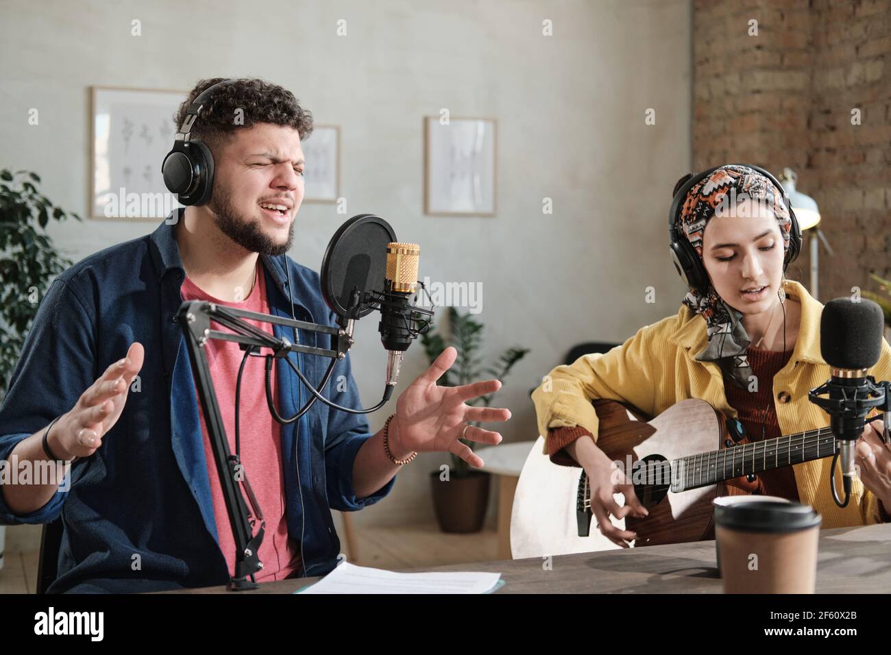 Young singer singing in microphone with young woman playing guitar in ...