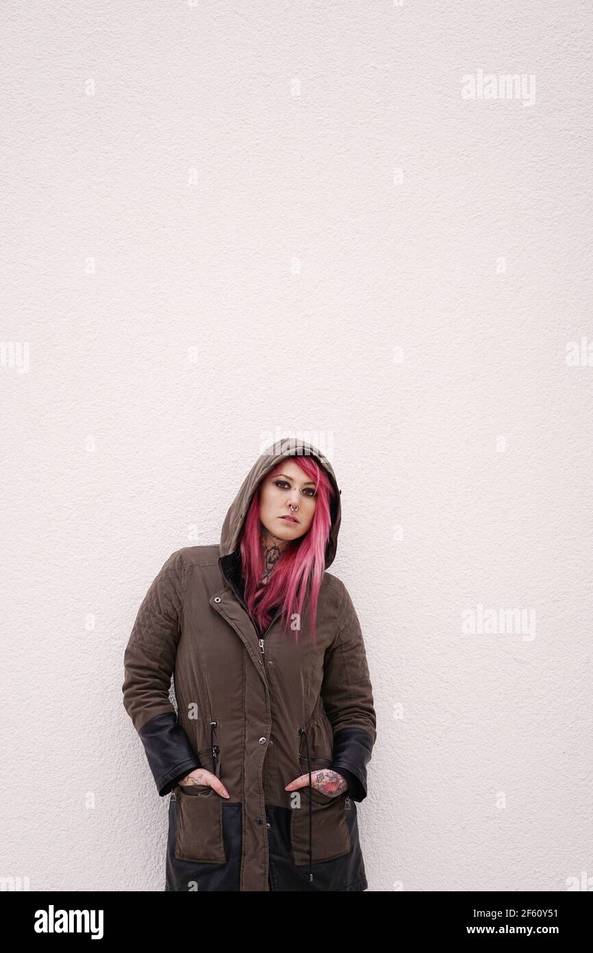 young woman with pink hair piercings and tattoos against wall with copy ...