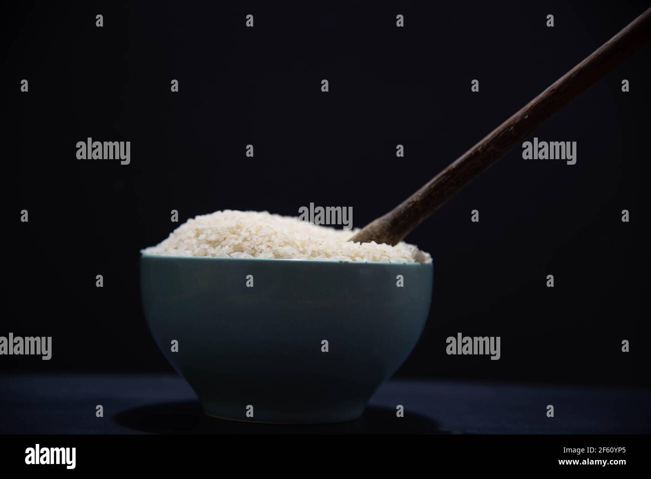 Porcelain pan with raw white rice and wooden spoon on black background ...