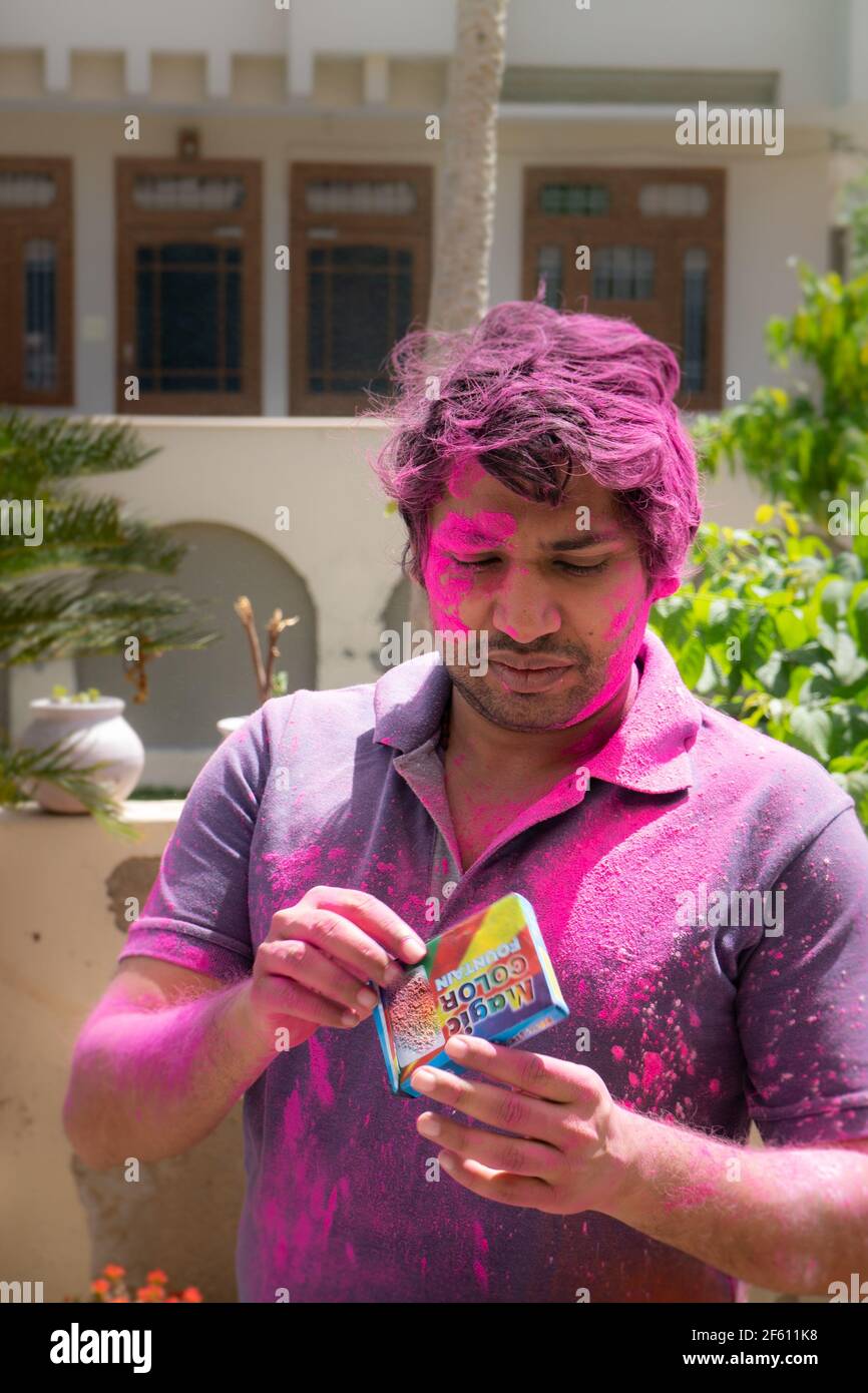 Young indian man covered in colored powder opening a packet of herbal ...