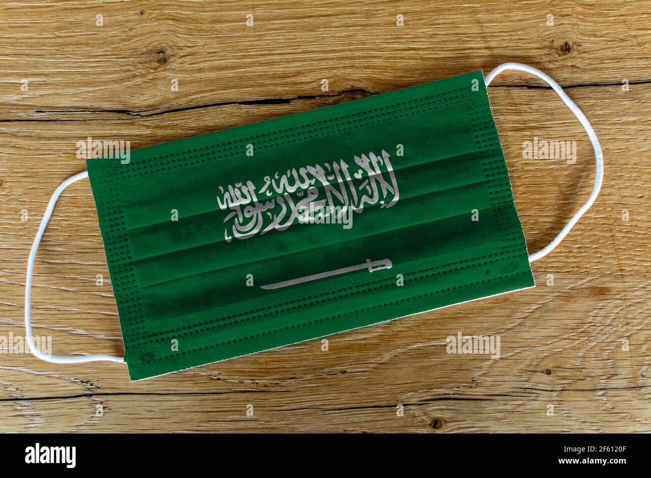 A surgical face mask with the painted flag of Saudia Arabia on a wooden ...