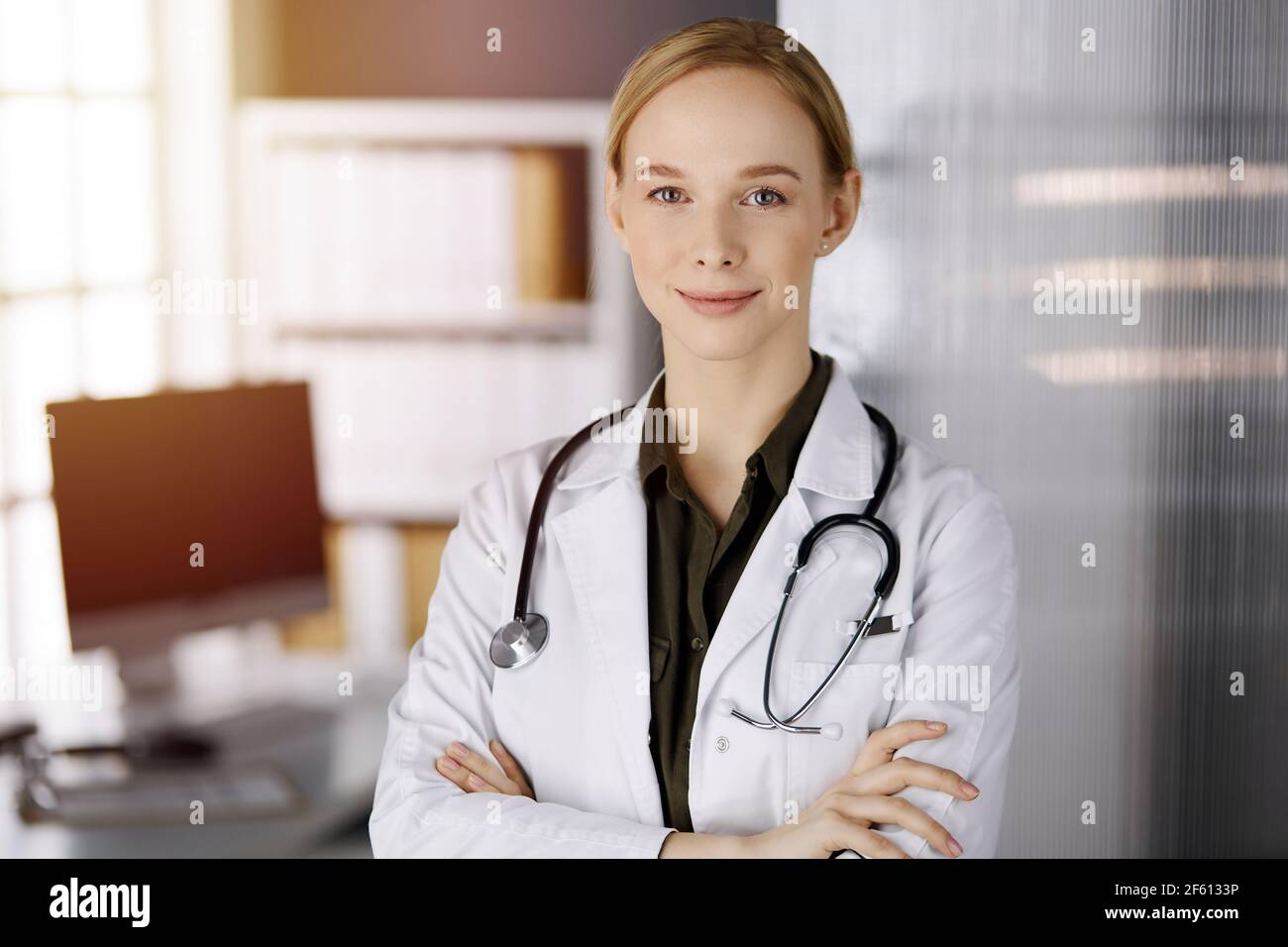 Cheerful smiling female doctor standing in sunny clinic. Portrait of ...