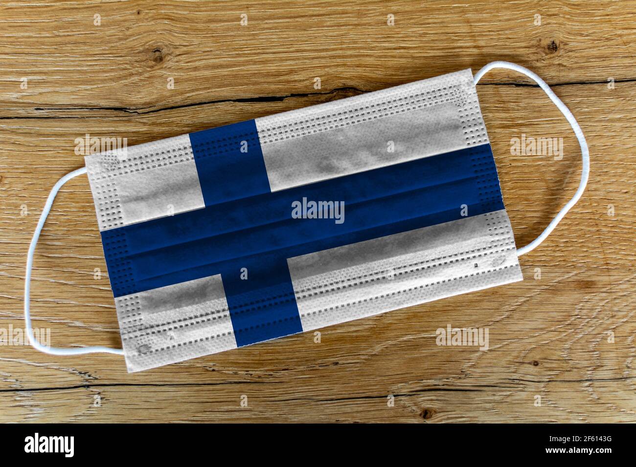 A surgical face mask with the painted flag of Finland on a wooden ...