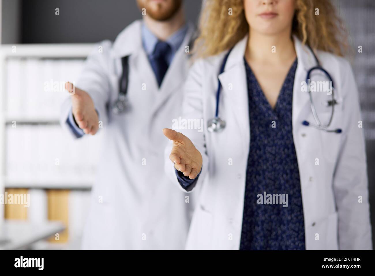 Two doctors standing and offering helping hand for shaking hand or ...