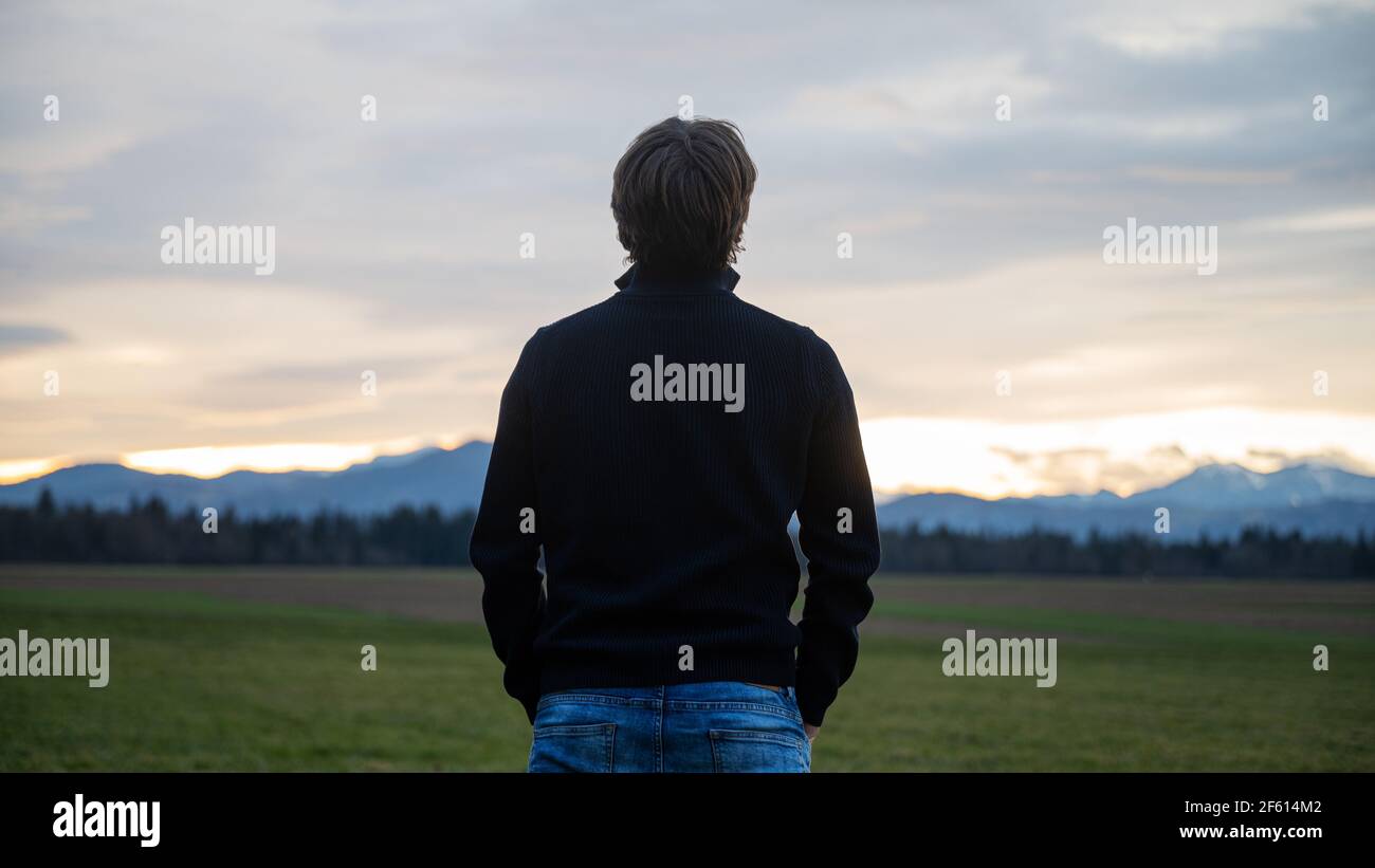 View from behind of a young man standing under a beautiful evening sky ...