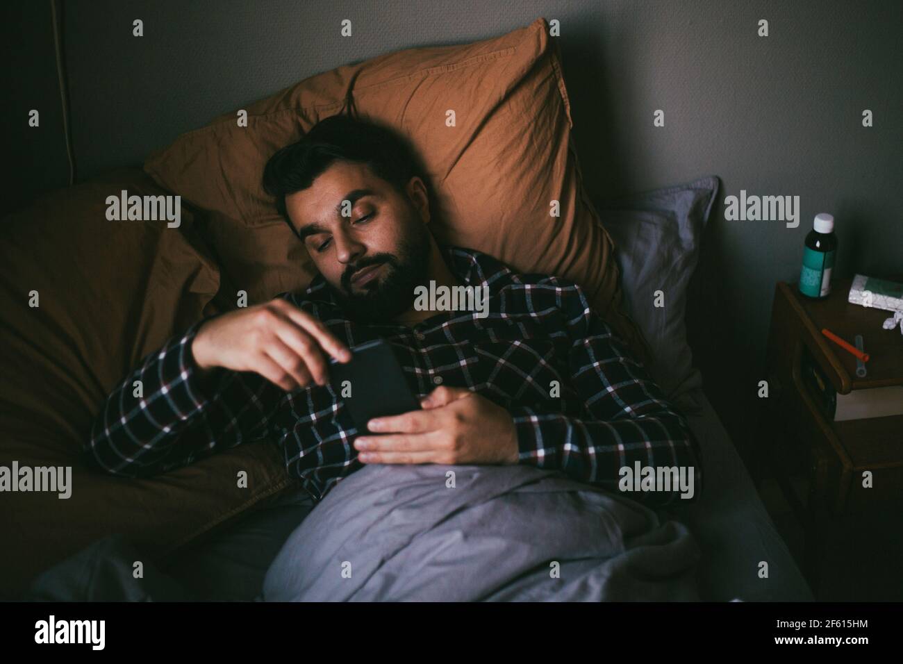 Sick man using smart phone while lying on bed at home Stock Photo - Alamy