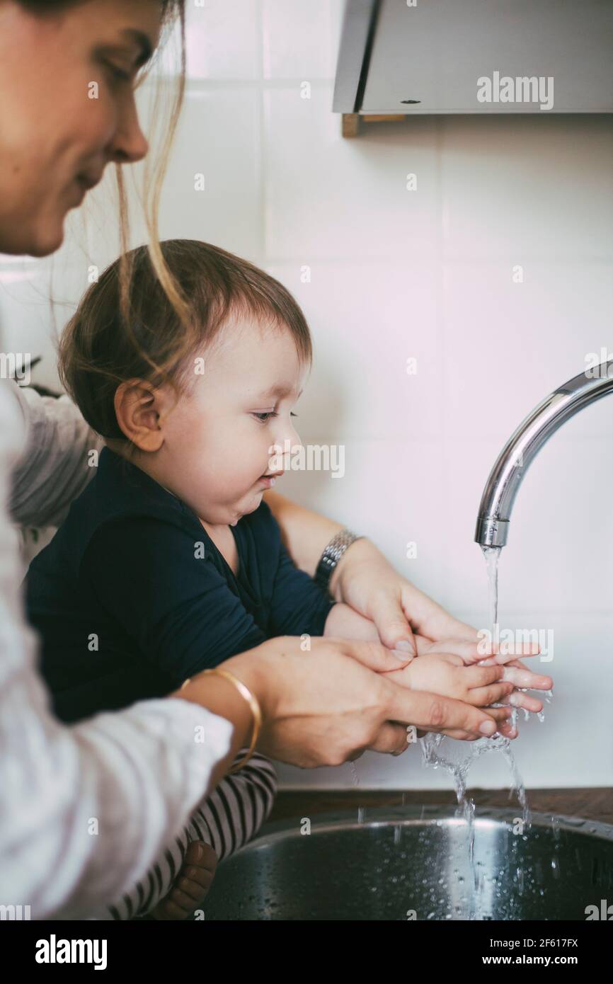 Mother helping baby girl washing hands under sink in kitchen Stock ...