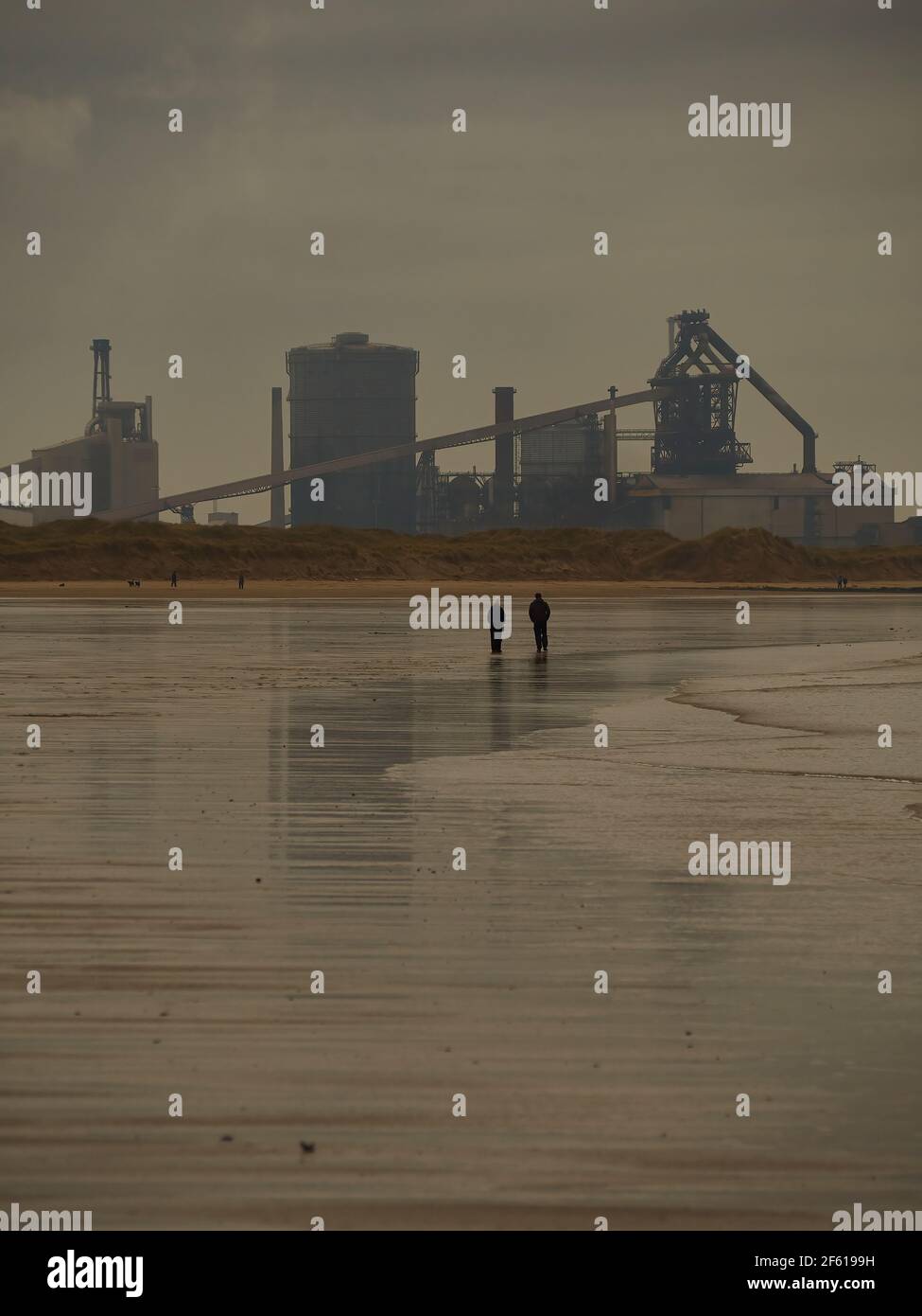 Bleached, stark landscape, a dull sky reflected on wet sand, two people ...