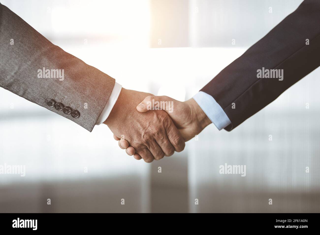 Business people standing and shaking hands in sunny office, close-up ...