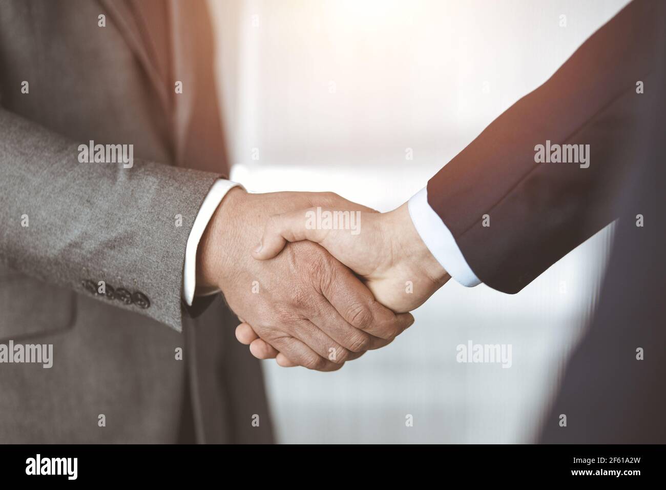 Business people standing and shaking hands in sunny office, close-up ...