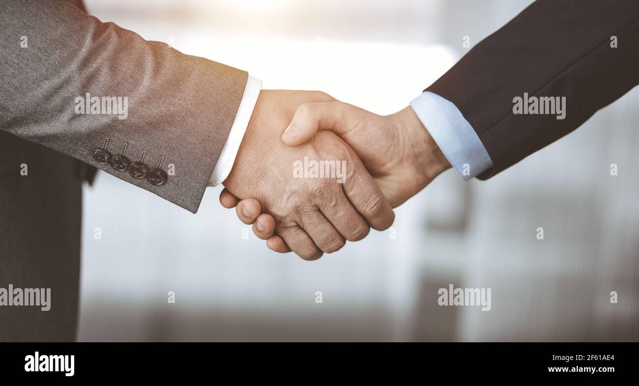 Business people standing and shaking hands in sunny office, close-up ...