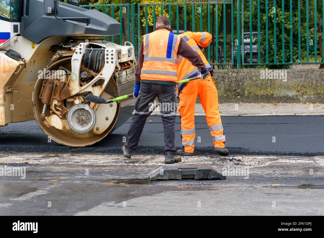 Paving workers add asphalt in front of wheel roller - road ...