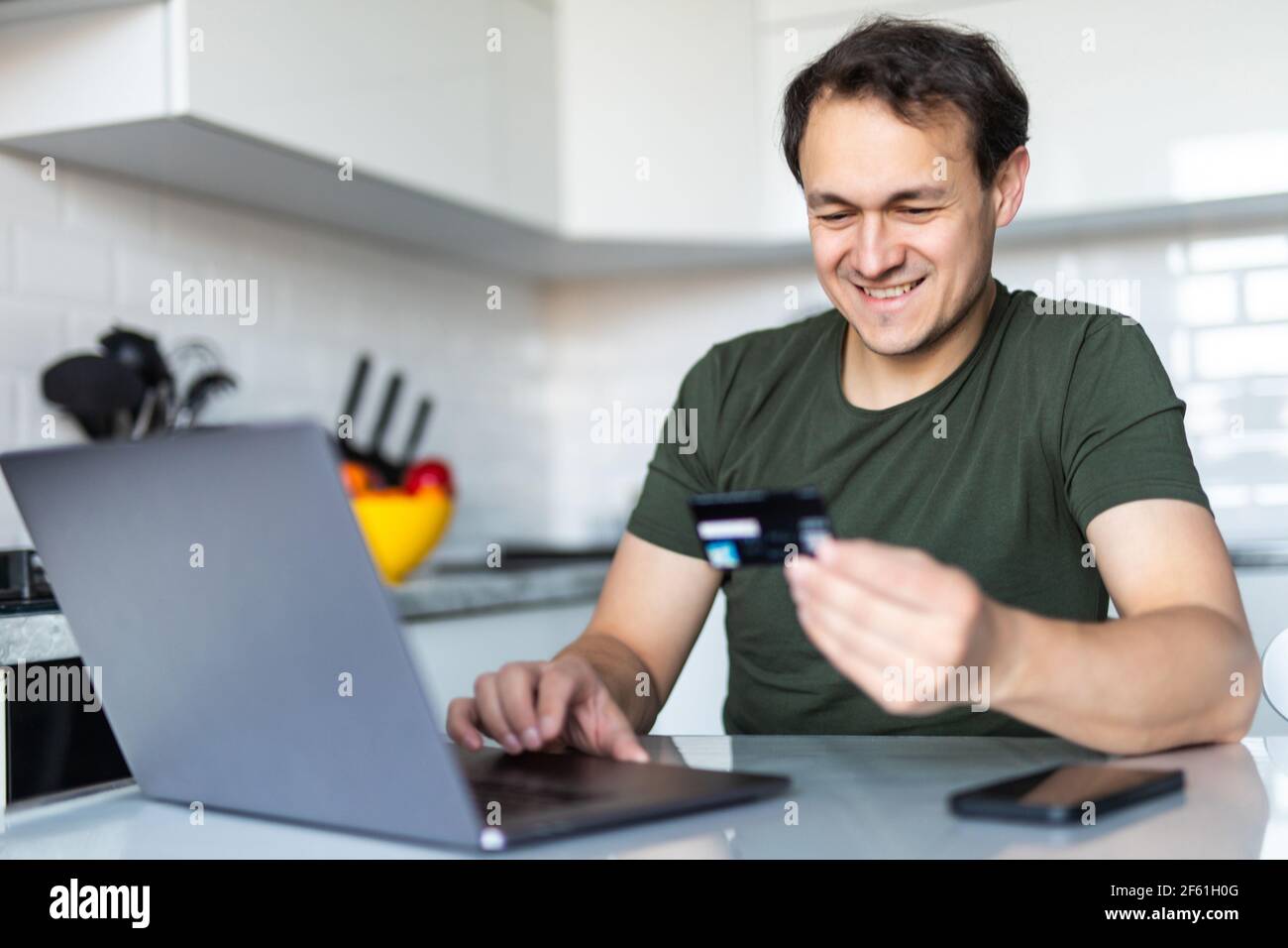 Happy young man using laptop computer while sitting at the kitchen ...