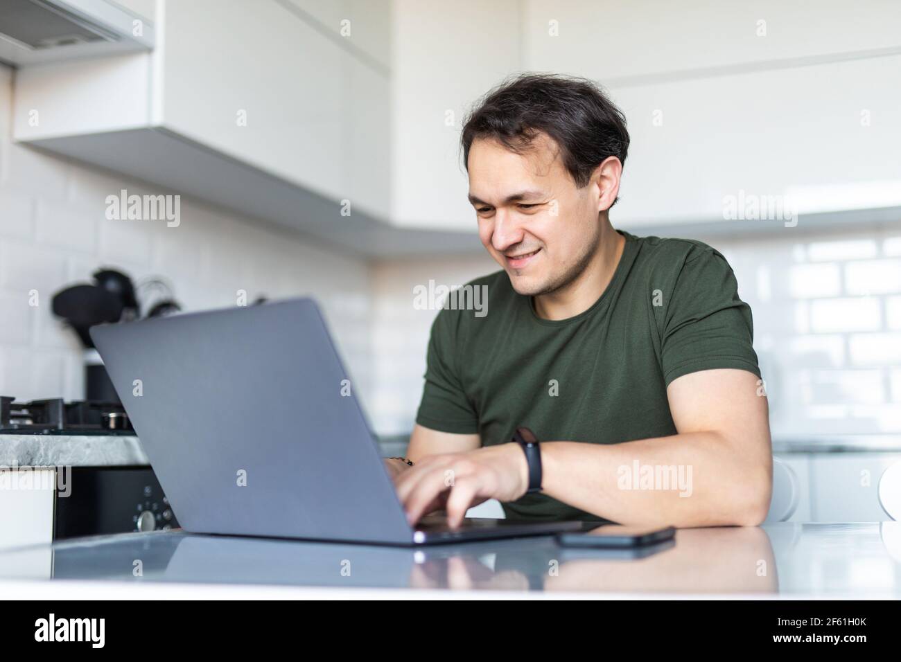 Handsome man using a laptop pc in the kitchen. Working from home in ...