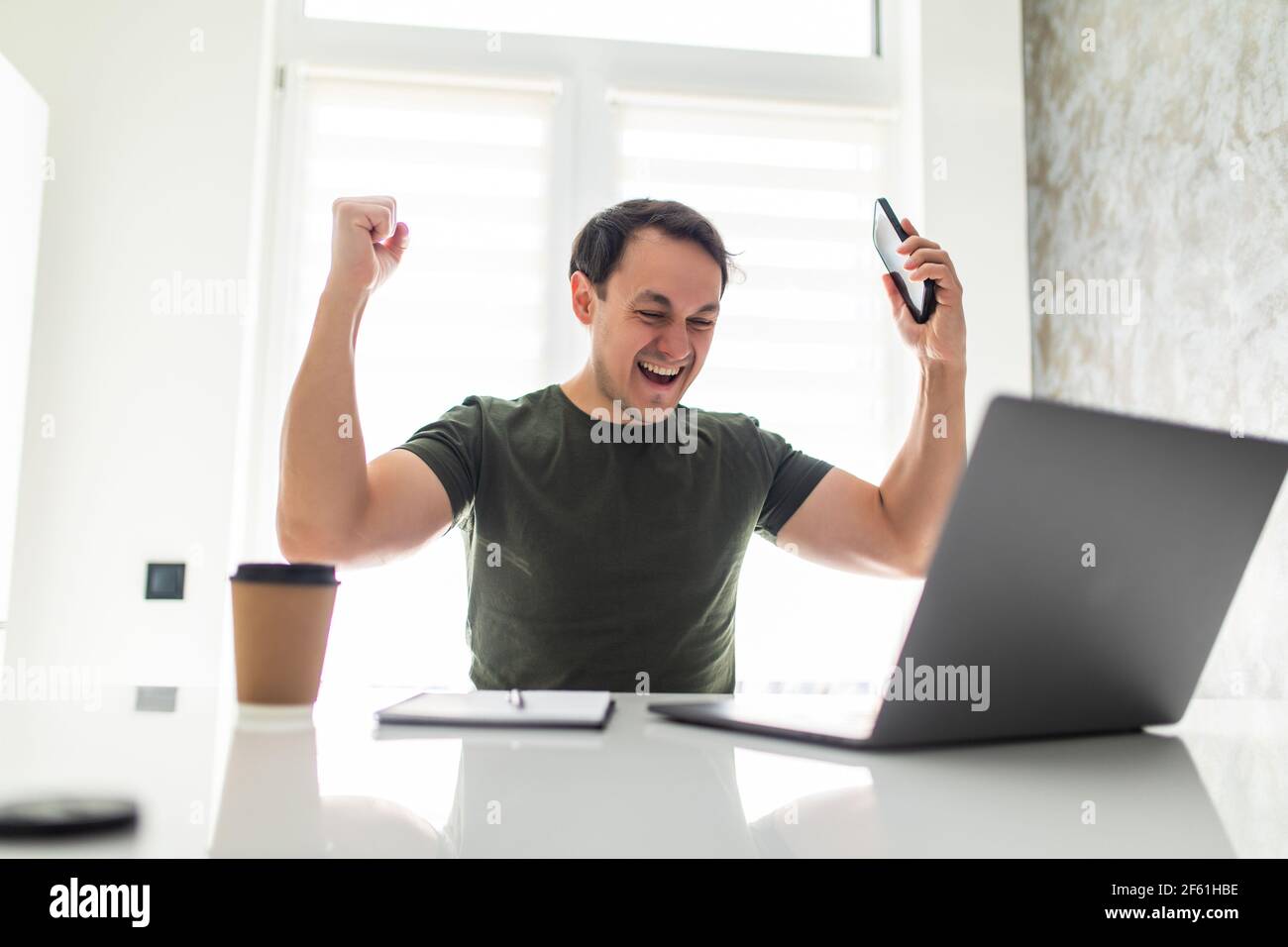 Overjoyed man wearing glasses using laptop in kitchen, showing yes ...