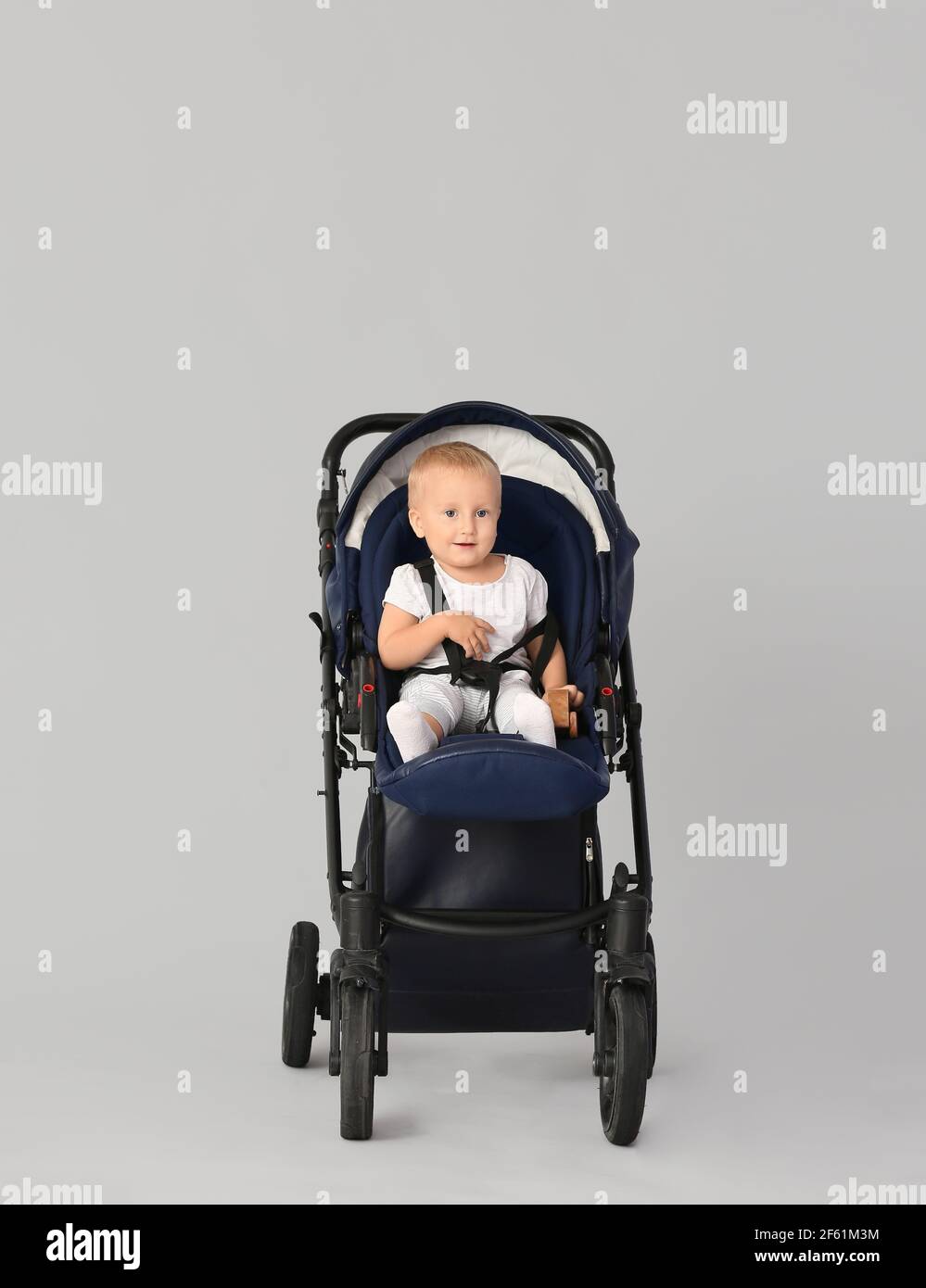 Cute funny baby in stroller on grey background Stock Photo - Alamy