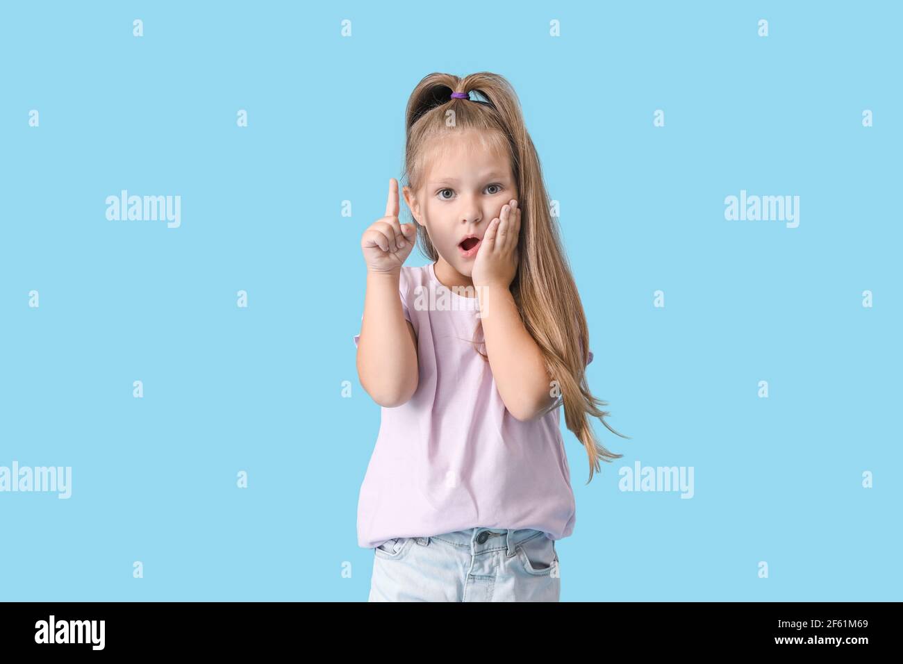 Surprised little girl with raised index finger on color background ...