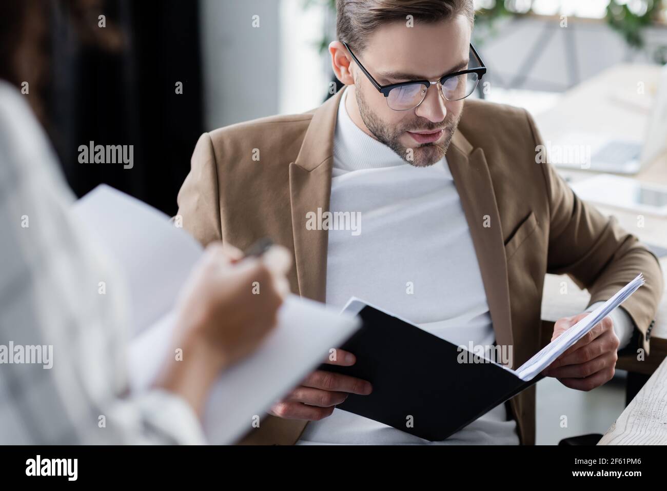 Businessman looking at documents near colleague with notebook on ...