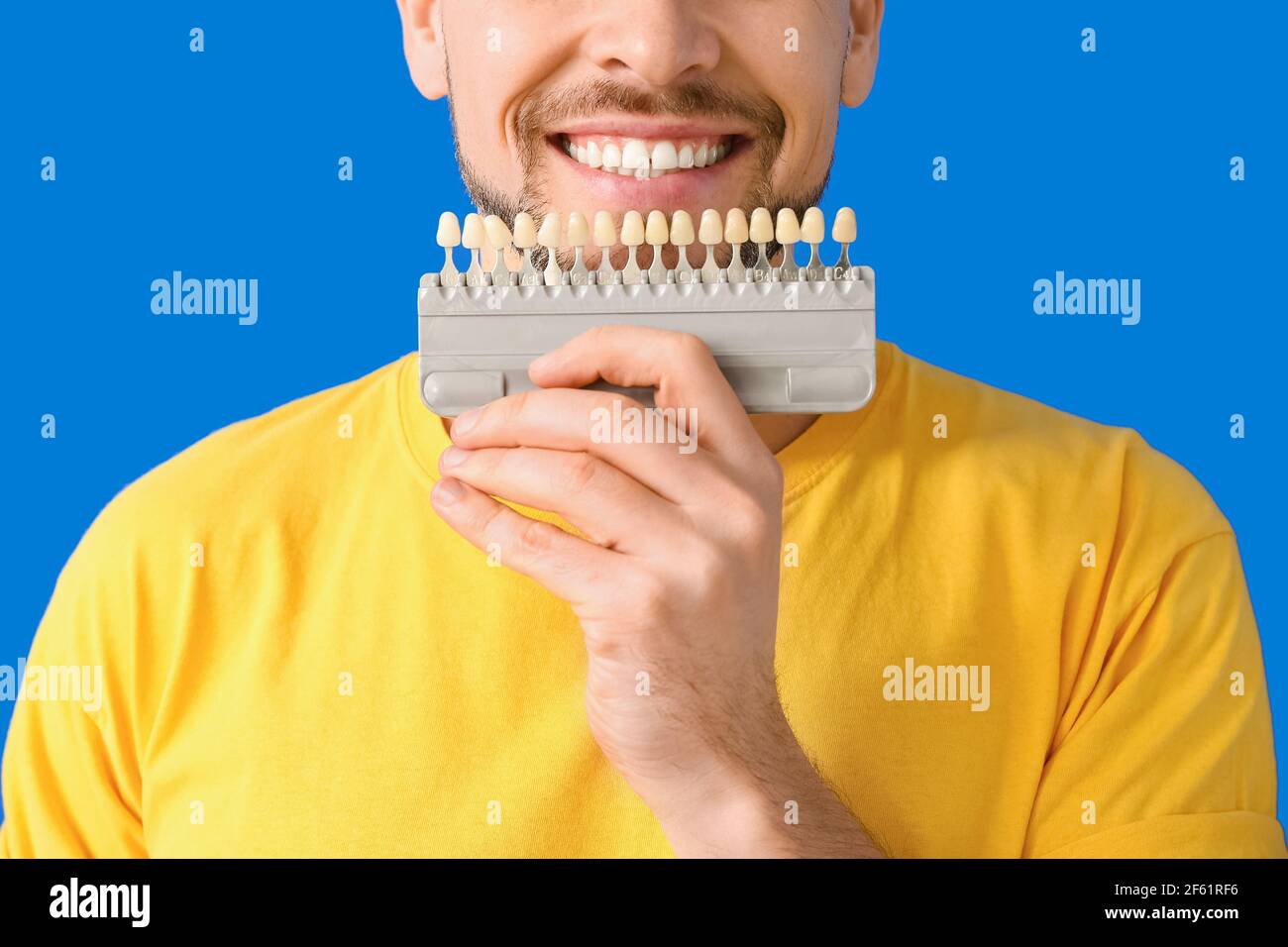 Man with teeth color chart on blue background, closeup Stock Photo - Alamy