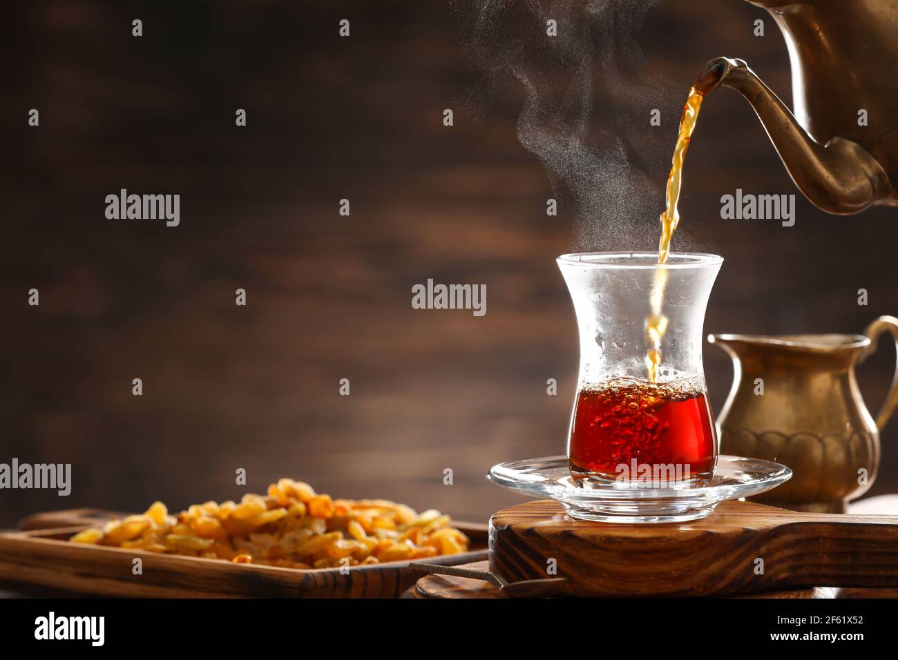 Pouring of hot Turkish tea from teapot into cup on wooden background ...