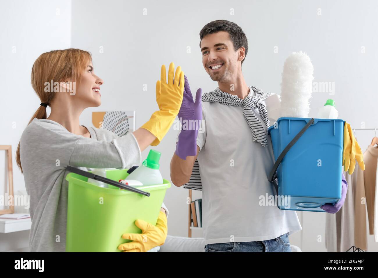 Young couple with cleaning supplies giving each other high-five at home ...