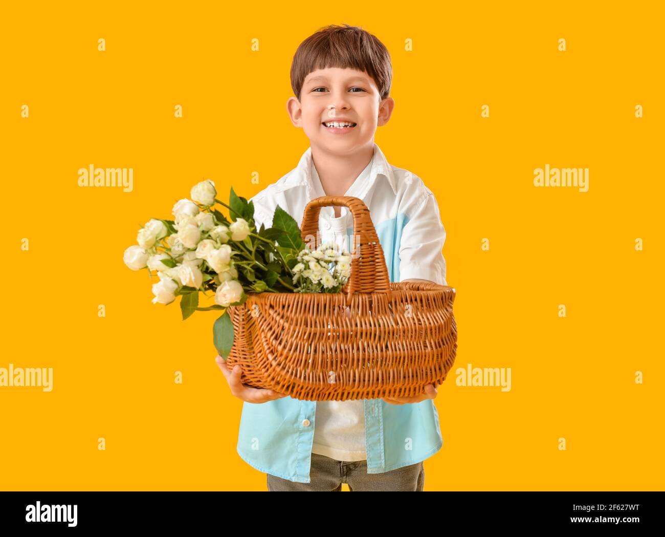 Cute little boy with bouquet of flowers in basket on color background ...