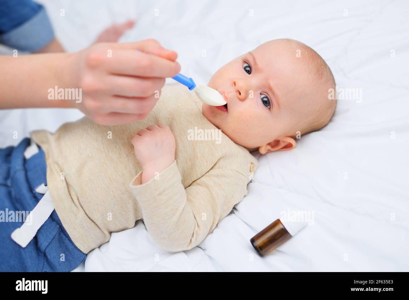 mother gives the child baby syrup from a small spoon on a white ...