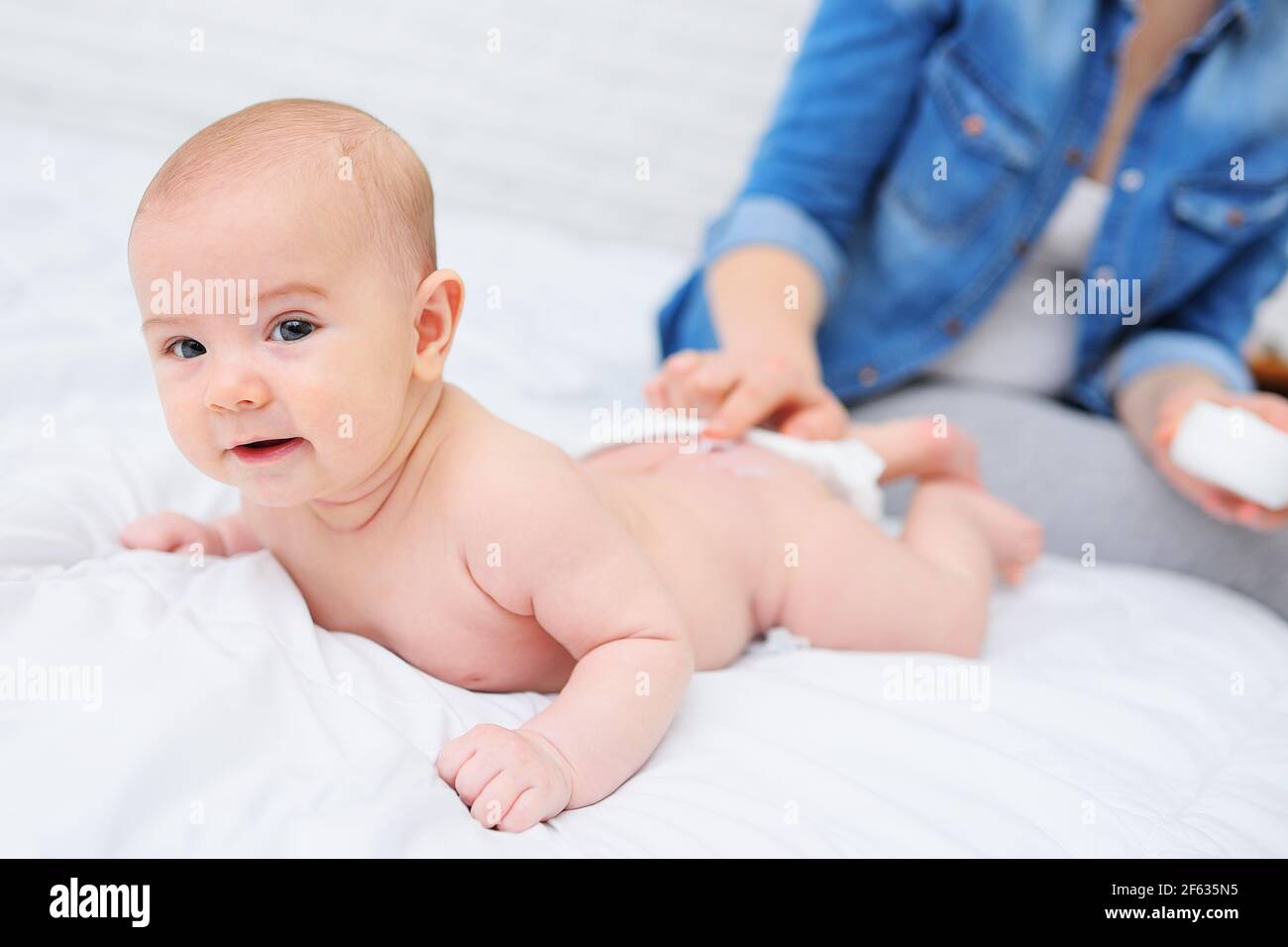 mother's hand applies a moisturizing baby cream to the baby boy's skin ...