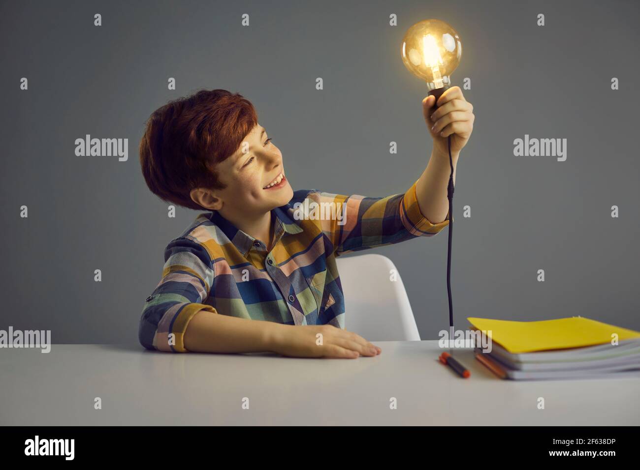 Happy creative student sitting at a school desk and holding a shining ...