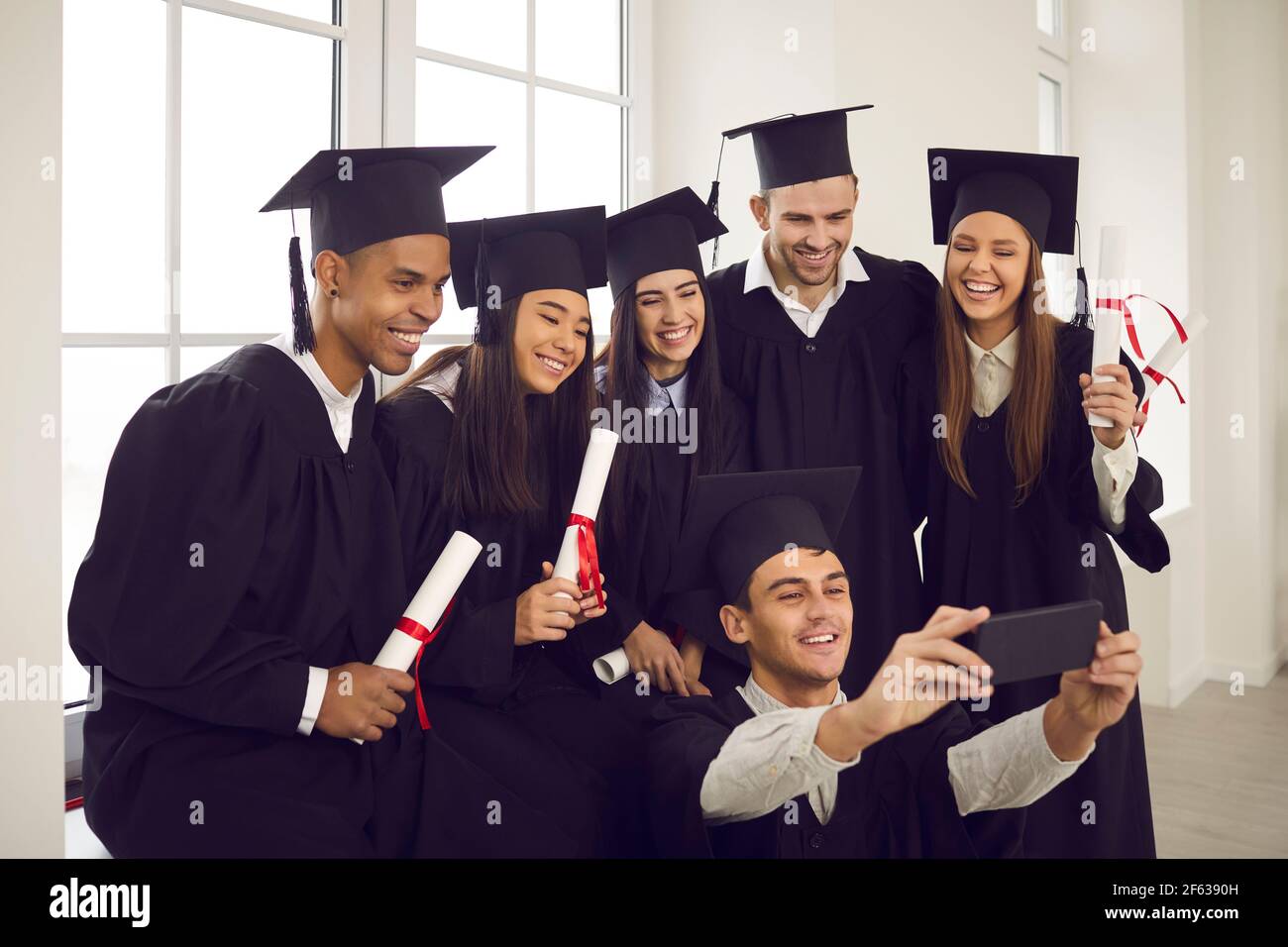 Group of happy international students with diplomas taking selfie using ...