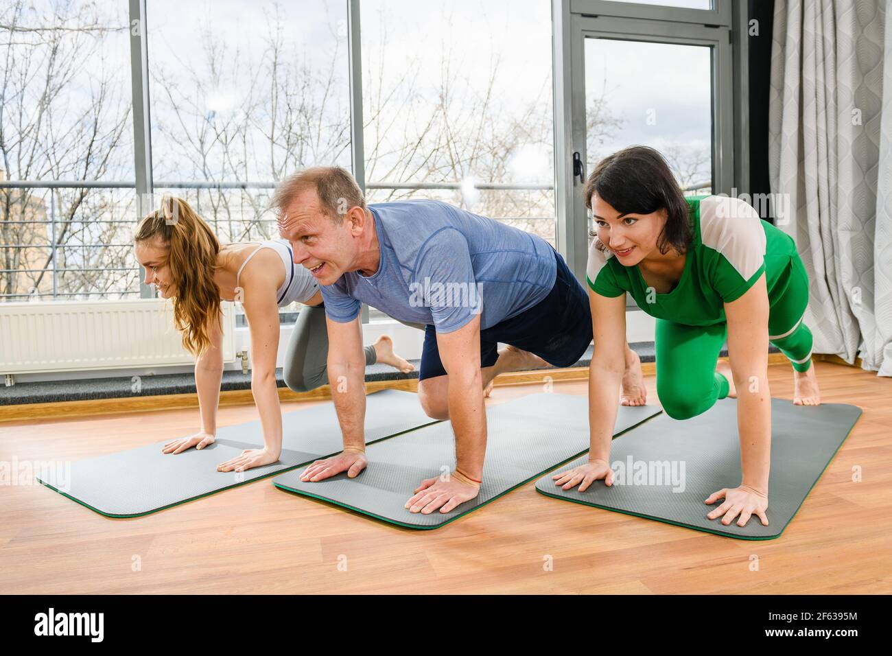 Three people different age stay on sport mat in plank position in light ...