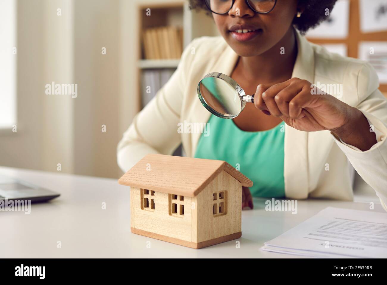 Real estate agent with a magnifying glass looking at a little house on ...