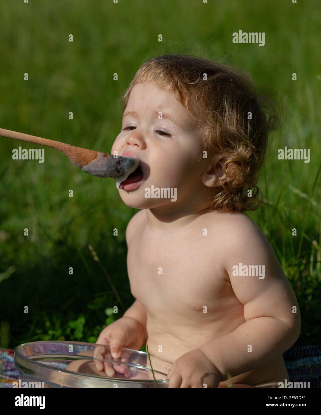 Spoon feeding baby. Funny baby in park eats herself with big wooden ...