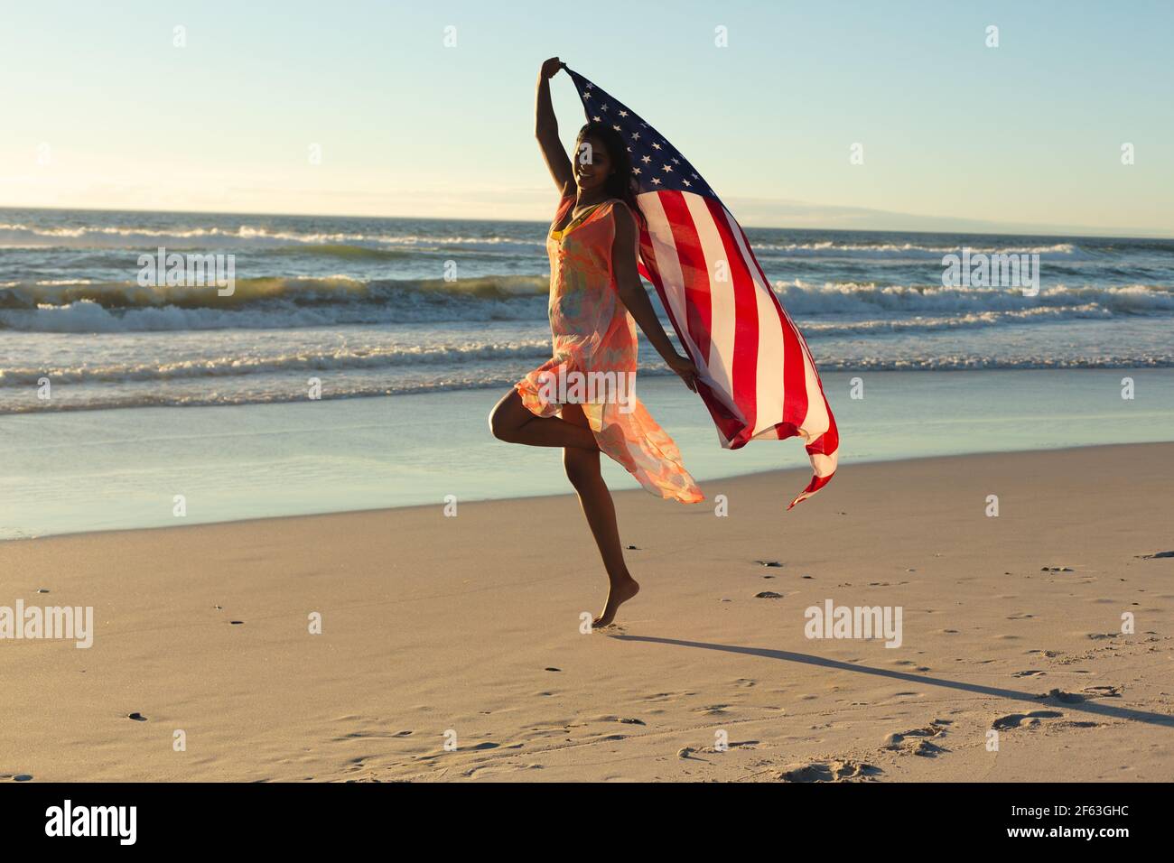 Mixed Race Patriotic Woman Jumping With American Flag On The Beach