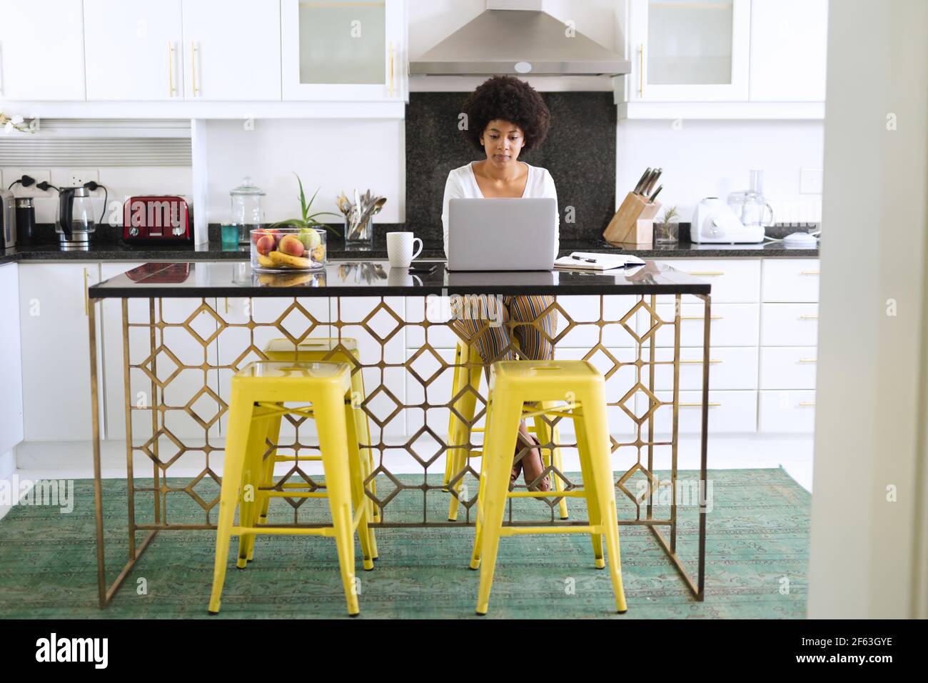 African american woman sitting in kitchen using laptop Stock Photo - Alamy