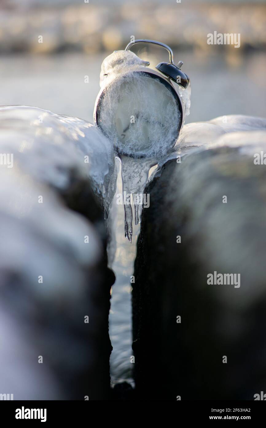 Time frozen alarm clock in ice on the beach between two rocks Stock ...