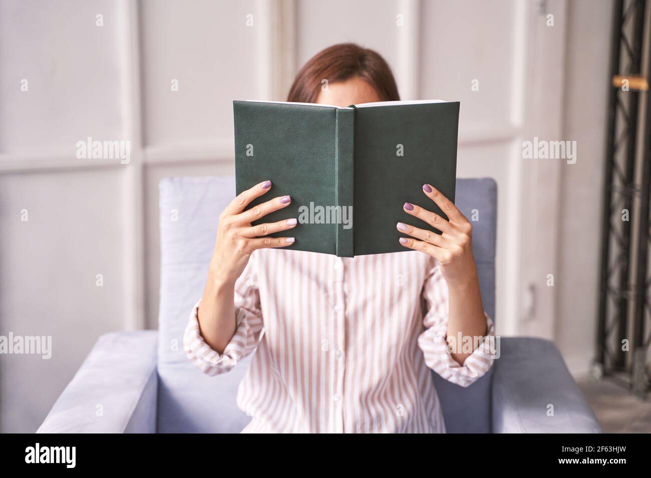 Young woman sitting at chair. Hide face behind notebook Stock Photo - Alamy