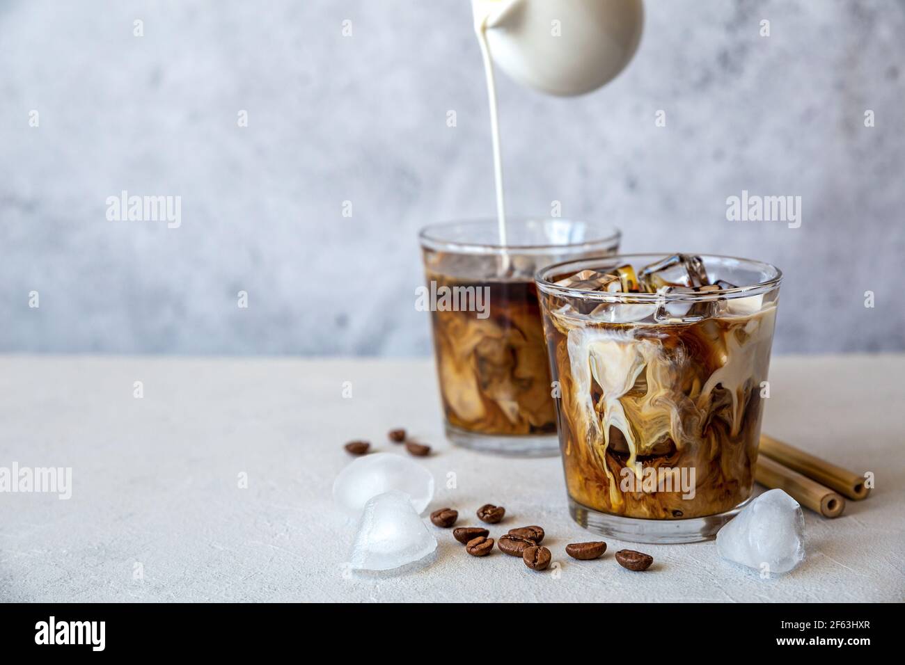 Two glass iced coffee with cream pouring from the top, ice cubes ...