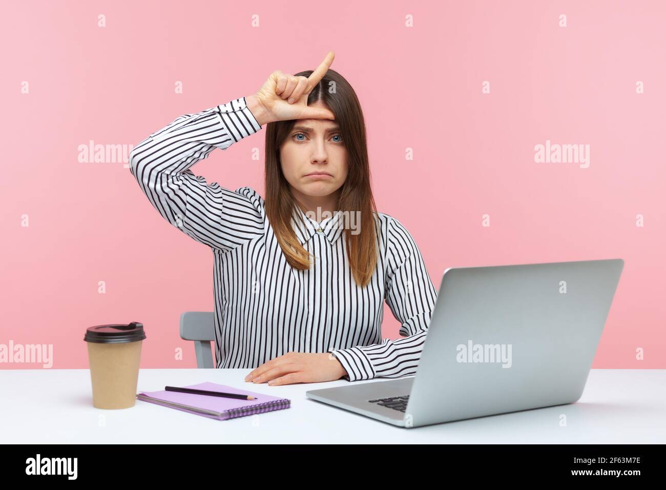Upset woman office worker showing loser gesture sitting at workplace ...